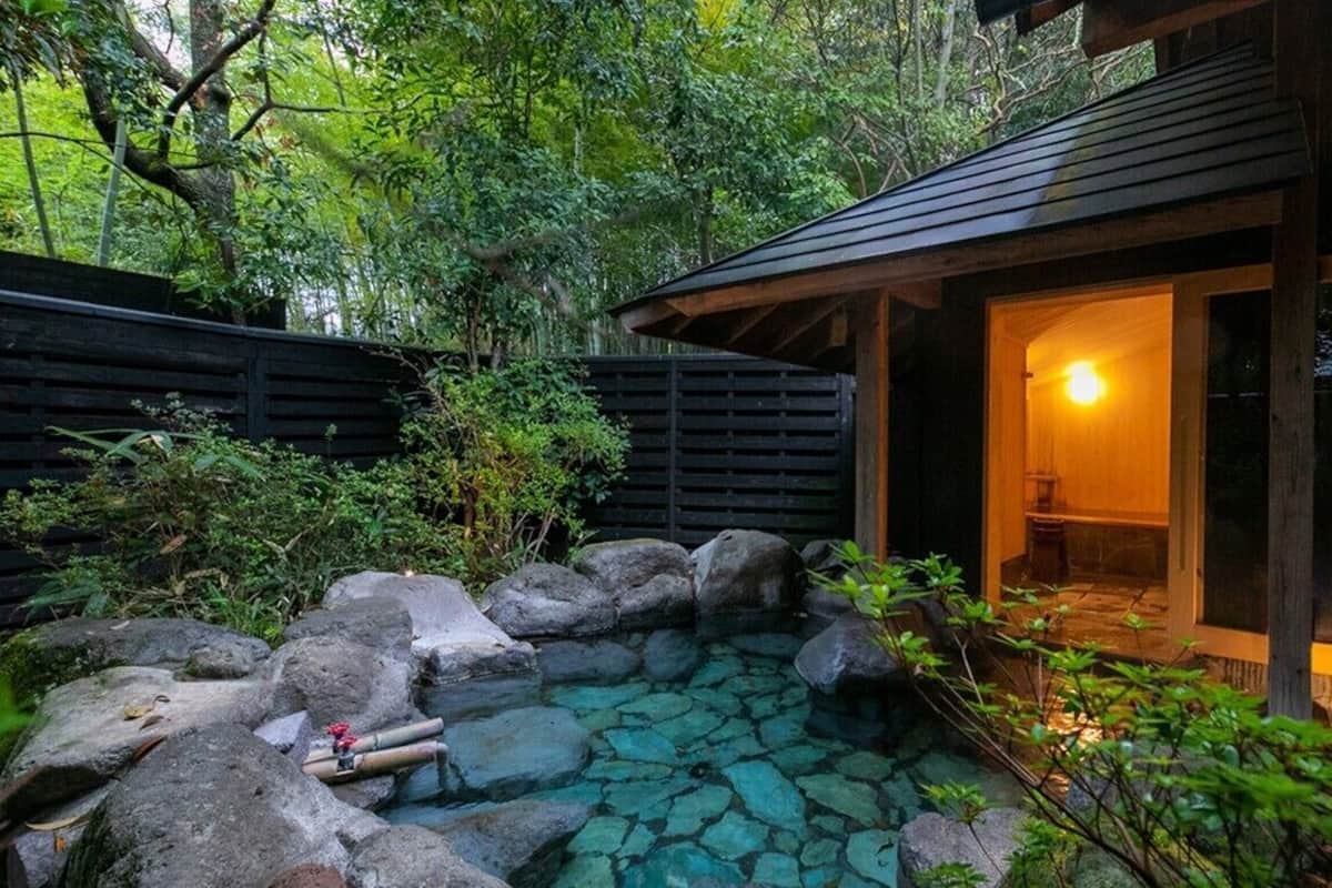 Um edifício em estilo japonês tradicional com lago de pedra, deck de madeira e interior iluminado.