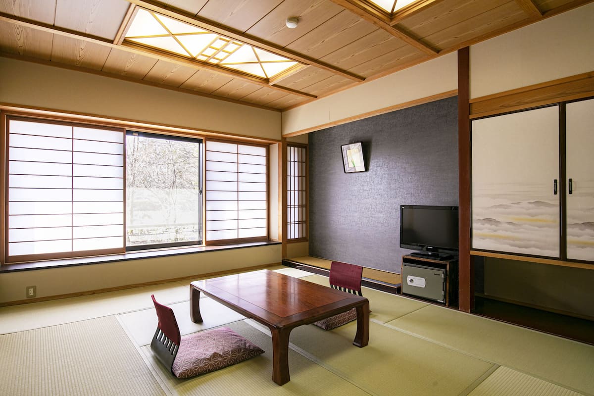 Um quarto japonês tradicional com tatames, uma mesa baixa, uma televisão e portas deslizantes.
