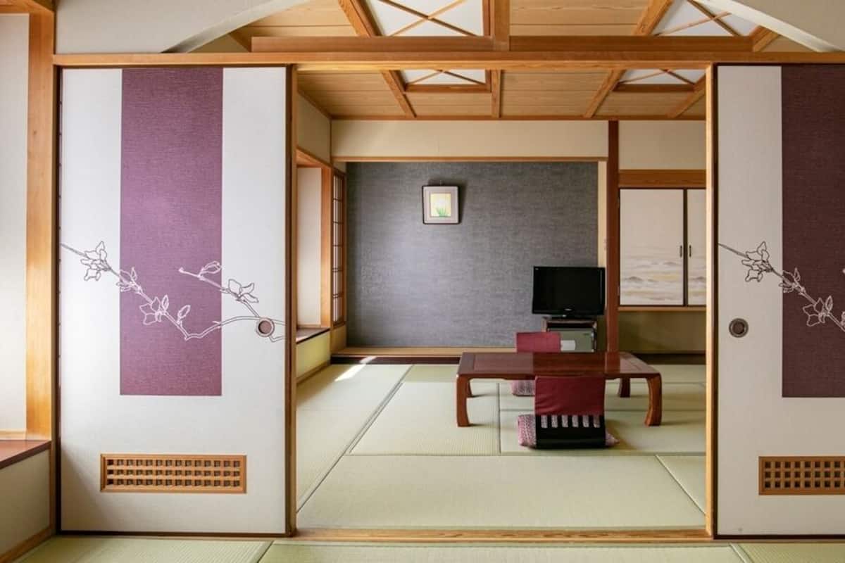 Um quarto japonês tradicional com tatames, uma televisão e uma mesa baixa com almofada vermelha.
