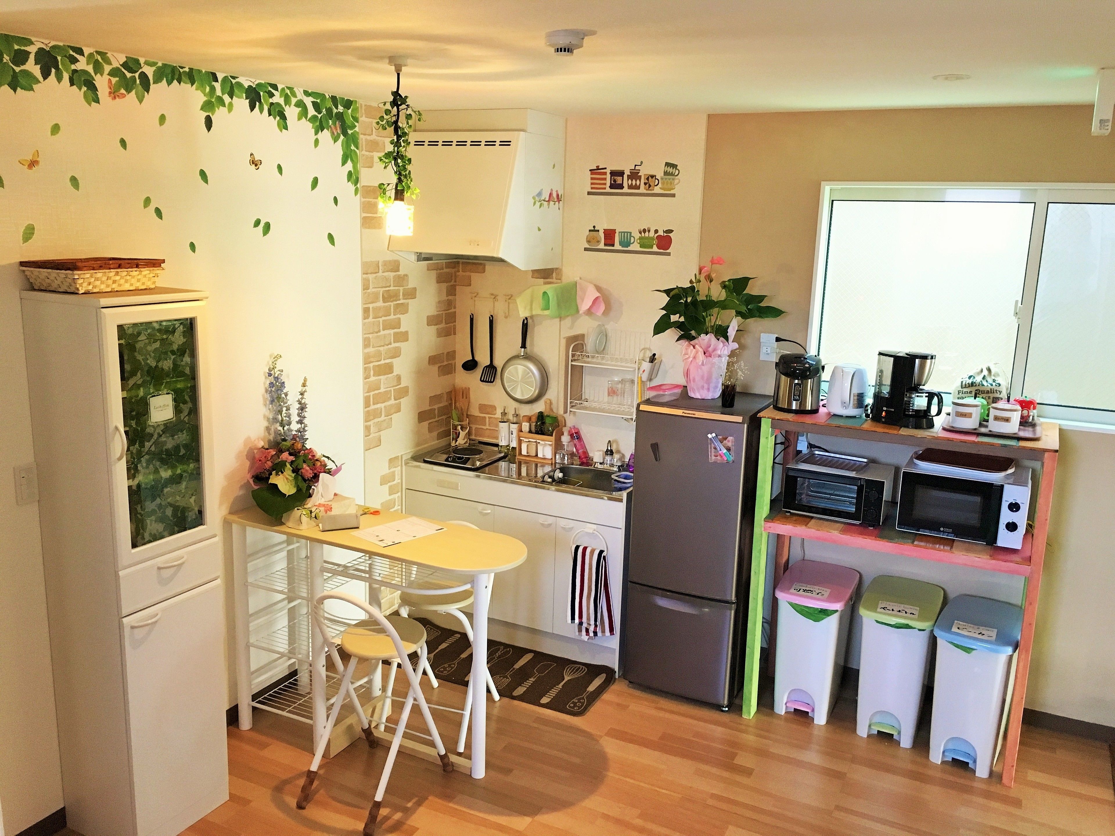 Uma cozinha compacta com geladeira, micro-ondas e pia. Há uma pequena área de refeições com mesa e cadeiras.