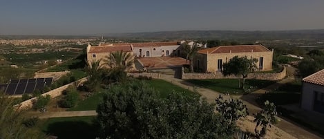 Um edifício de pedra tradicional com um pátio, rodeado por vegetação e vista para o campo.