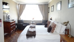 Quarto de hotel com uma cama grande, duas poltronas, uma mesinha e um aparador.