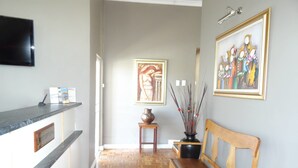 Uma área de recepção com balcão de mármore, um banco de madeira, um vaso com ramos decorativos e duas obras de arte emolduradas na parede.