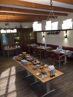 Uma área de refeições com mesas e bancos de madeira, um buffet com alimentos e uma pintura de cavalos na parede.