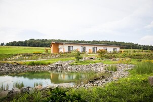 Um edifício térreo com telhado plano, inserido em paisagem natural com lago e vegetação.