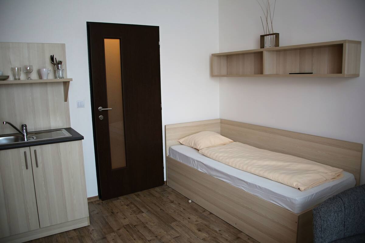 Quarto compacto com cozinha compacta, uma cama e prateleira de madeira.