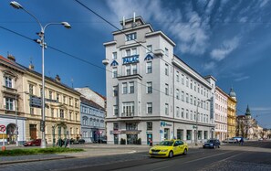 Um hotel com vários andares, com uma placa grande 'PALACE', um 'CAFE PALAC' no andar térreo e uma placa 'HOTEL PALACE' na esquina.