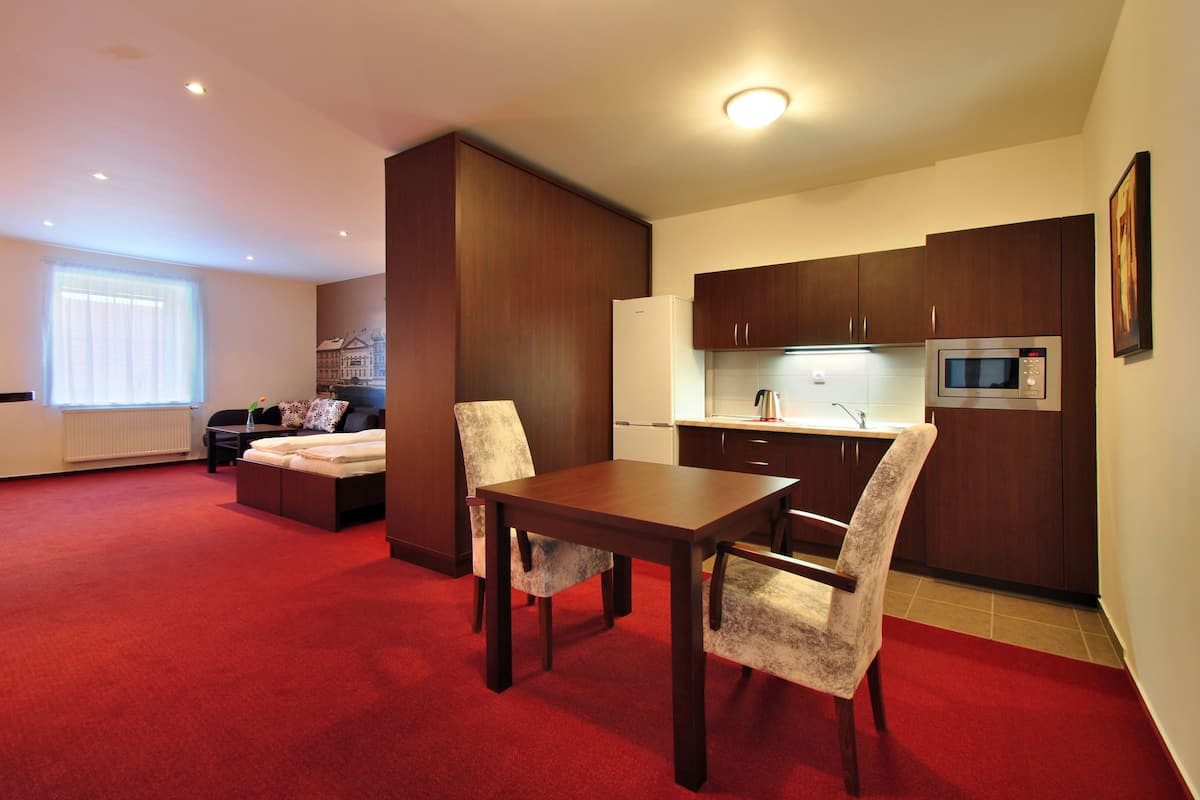 Quarto compacto com mesa de jantar, duas cadeiras, sofá, cozinha compacta e uma janela grande com persianas.