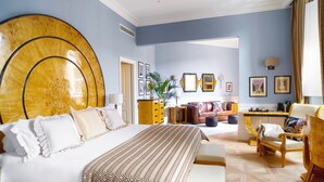 Um quarto de hotel espaçoso, com uma cama grande, uma área de estar com sofá e poltronas, e um espaço de jantar com mesa e cadeiras.