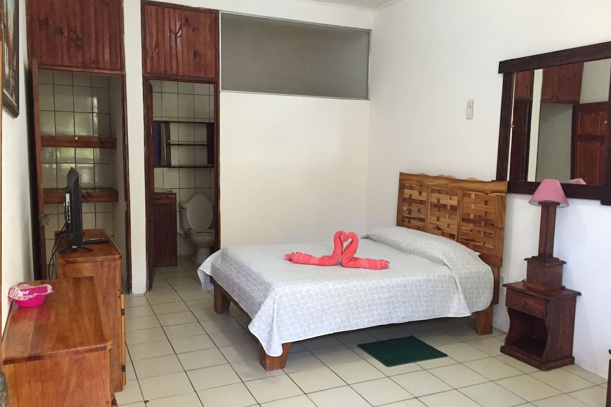 Quarto com cama, guarda-roupa de madeira, secretária, espelho e casa de banho.