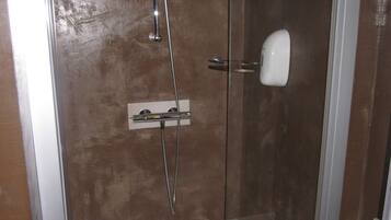 Box de chuveiro envidraçado com chuveiro manual e acessórios manuais, incluindo um dosador de sabonete fixado em um suporte de parede.