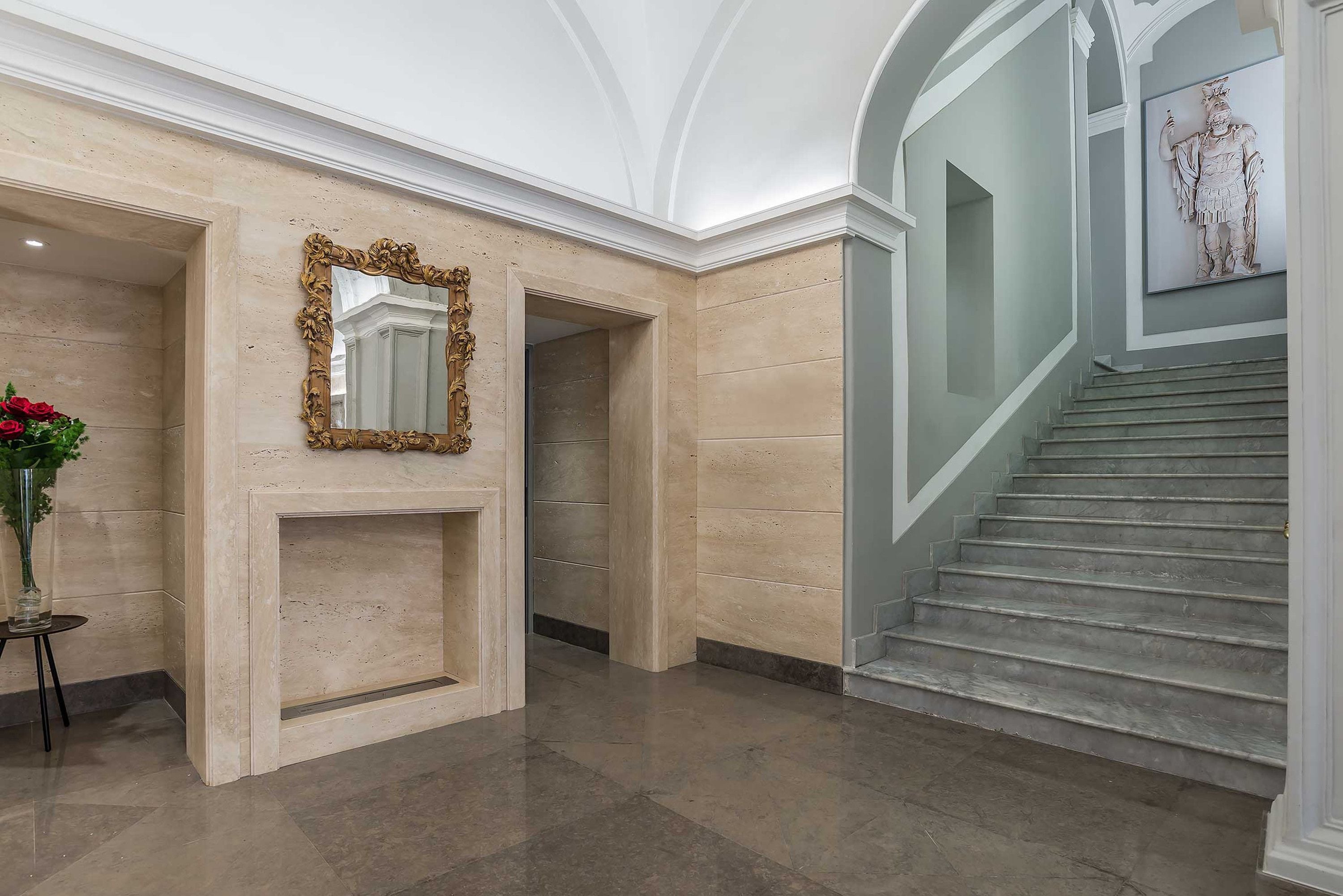 Um hall imponente com piso de mármore, um espelho grande e uma escadaria que dá acesso a um andar superior.