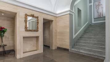 Um hall imponente com piso de mármore, um espelho grande e uma escadaria que dá acesso a um andar superior.