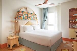 Uma cama bem arrumada com cabeceira estampada em padrão geométrico, mesa de cabeceira de madeira com telefone e um ventilador de teto.