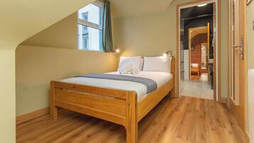 Quarto com cama de madeira, janela com cortinas e vista para um banheiro com espelho e pia.