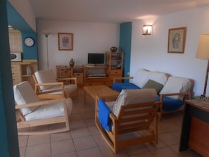 Uma sala de estar com sofá, cadeiras, televisão e uma pequena mesa.