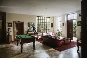 Uma sala de estar ampla com mesa de bilhar, sofá de couro e grandes janelas que proporcionam luz natural.