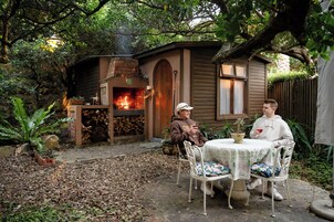 Uma área de estar ao ar livre rústica, com forno de tijolos, mesa de madeira e cadeiras.
