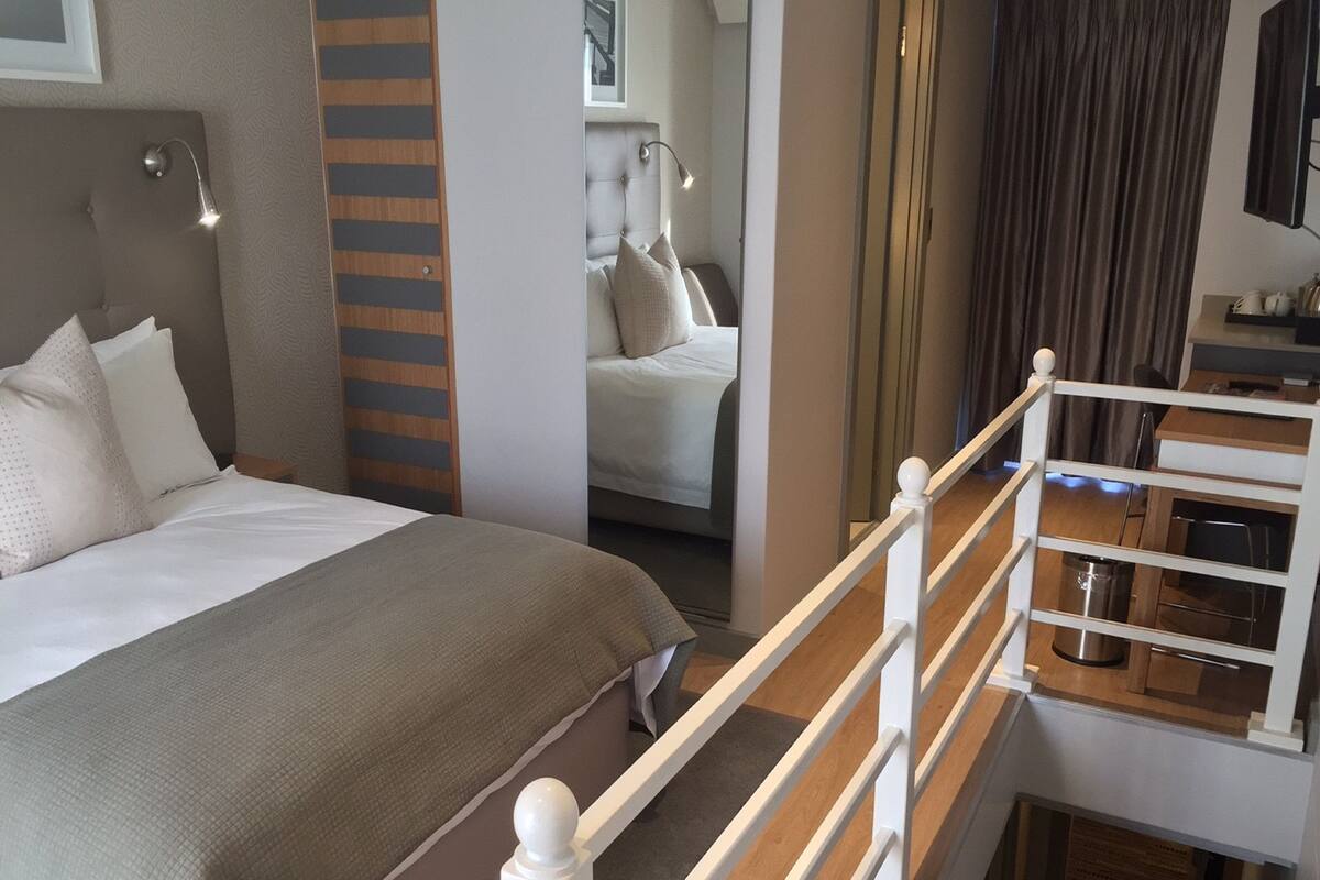 Quarto de hotel com cama, mesa de cabeceira e escrivaninha com cadeira.
