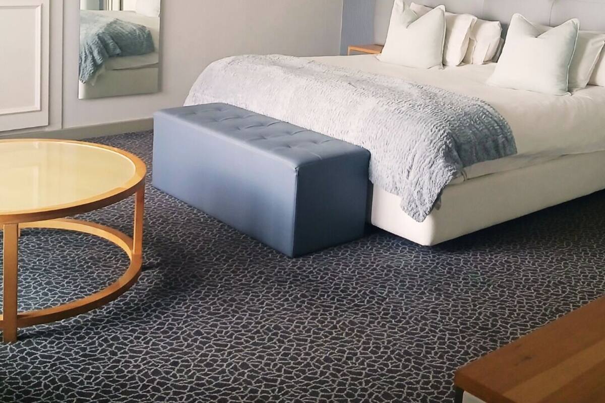 Quarto moderno com cama grande, mesa de cabeceira, mesa de centro redonda e um banco.
