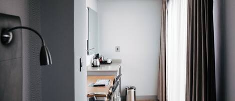 Quarto de hotel moderno com cozinha compacta, área de refeições e uma grande janela com cortinas.