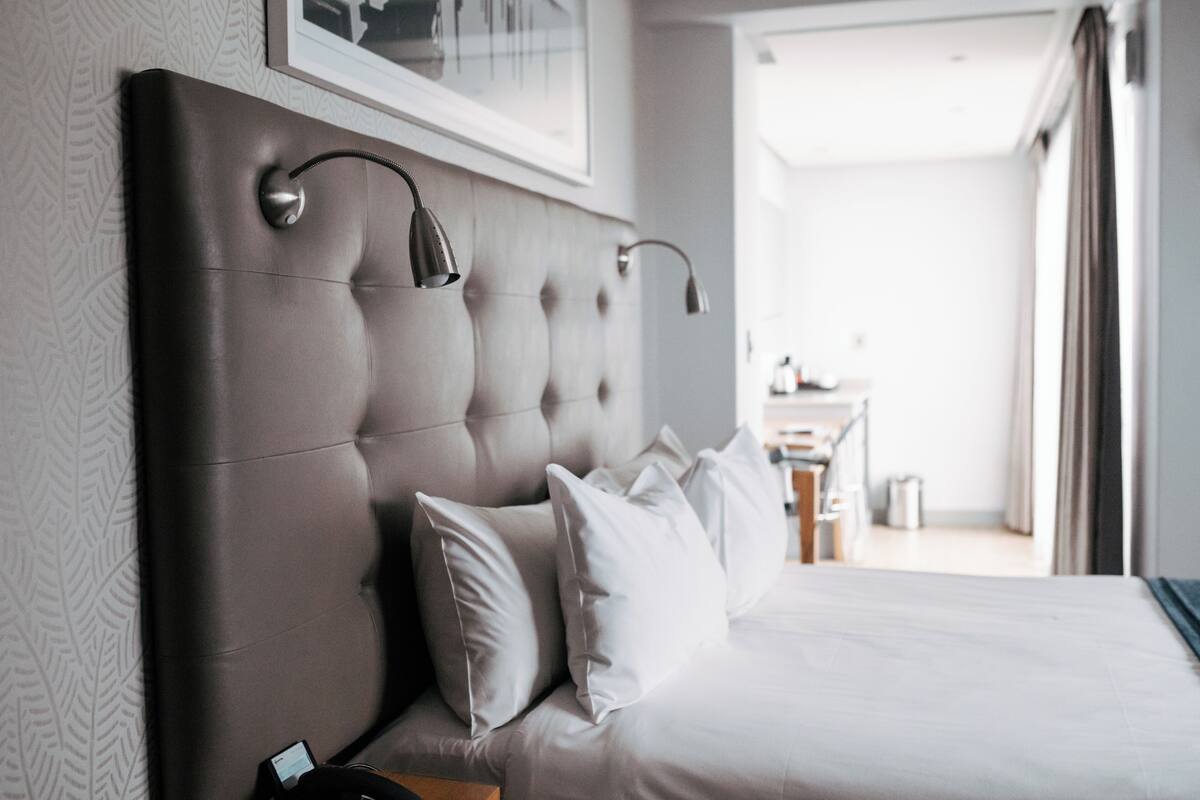Cama bem arrumada com roupa de cama branca e cabeceira acolchoada.