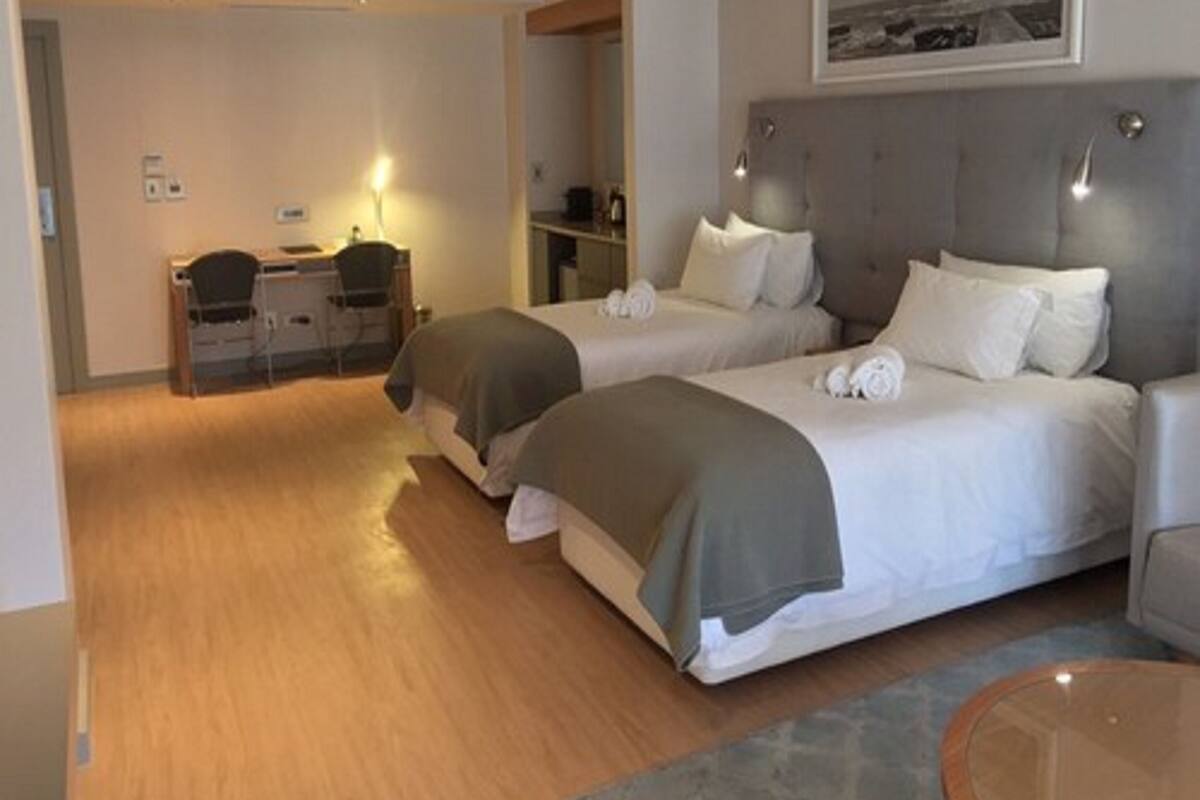 Quarto de hotel com duas camas, uma escrivaninha e uma cadeira.