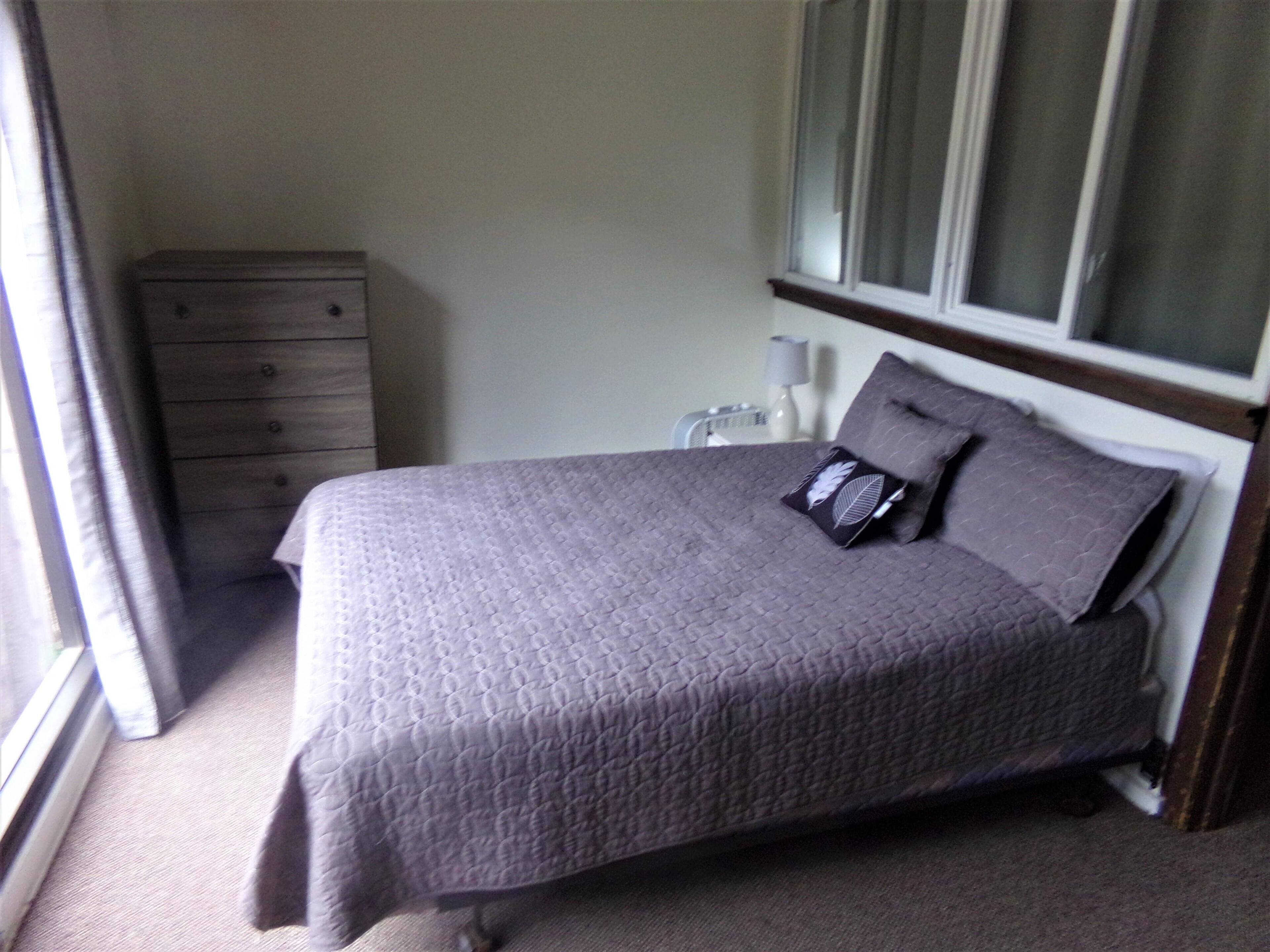 Quarto com cama, cómoda, janela e mesa de cabeceira com abajur.