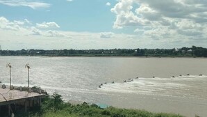 Um rio com barcos, um cais e uma linha de costa distante com edifícios.