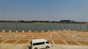 Uma van branca estacionada numa área pavimentada, com vista para a água e a costa ao longe.