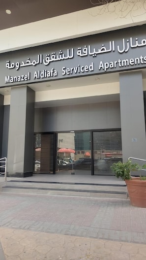 Exterior dos Apartamentos Manazel Aldiafa Serviced, com entrada moderna e um grande vaso de planta.