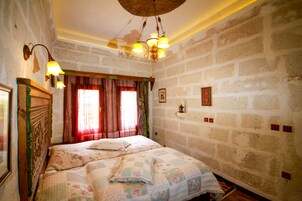 Quarto com parede de tijolos, cama de madeira com roupa de cama floral, lustre pendurado e um quadro na parede.