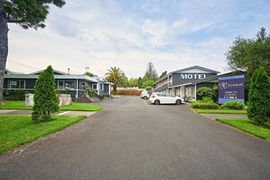 Um motel com placa, um carro estacionado e um gramado bem cuidado.