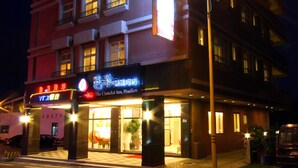 Um hotel de vários andares com janelas iluminadas e um letreiro de neon anunciando The Camelot Inn.