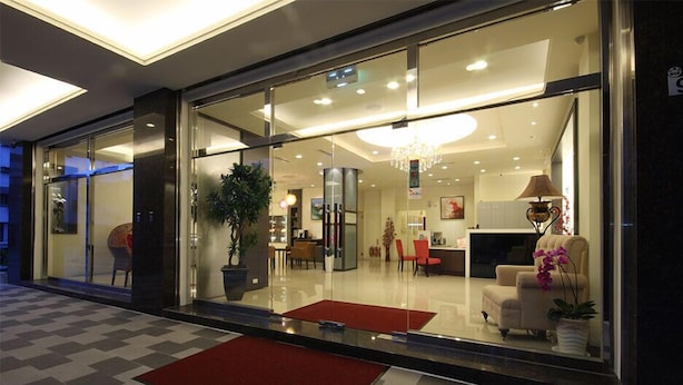 Um lobby moderno de hotel com piso xadrez, balcão de recepção e área de estar com cadeiras e um sofá.