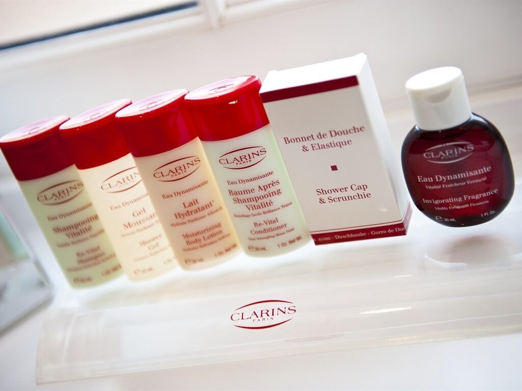 Exposição de produtos Clarins Paris, incluindo touca de banho, elástico de cabelo e diversos shampoos e condicionadores.