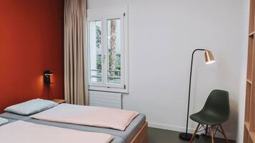 Quarto com duas camas, janela com cortinas, luminária de chão e uma cadeira.