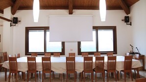 Uma sala de conferências com uma mesa grande, cadeiras de madeira, uma tela de projetor e janelas amplas com vista.