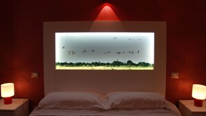 Quarto com cama, duas luminárias de cabeceira e TV na parede exibindo uma paisagem natural.