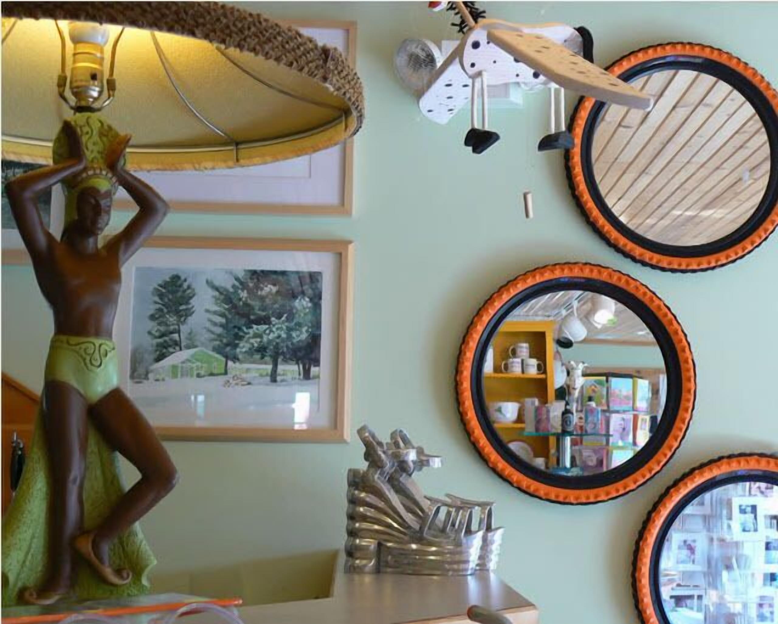 Quarto com escultura de madeira, obra de arte emoldurada e vários espelhos com bordas laranja.