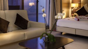 Quarto de hotel com sofá, uma mesinha com um vaso de flores, cama e mesa de cabeceira com abajur.