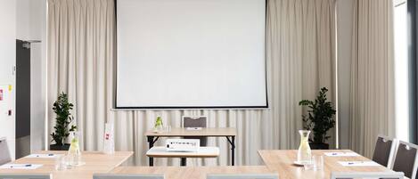 Uma sala de conferências com uma tela de projeção grande, mesas e cadeiras de madeira.