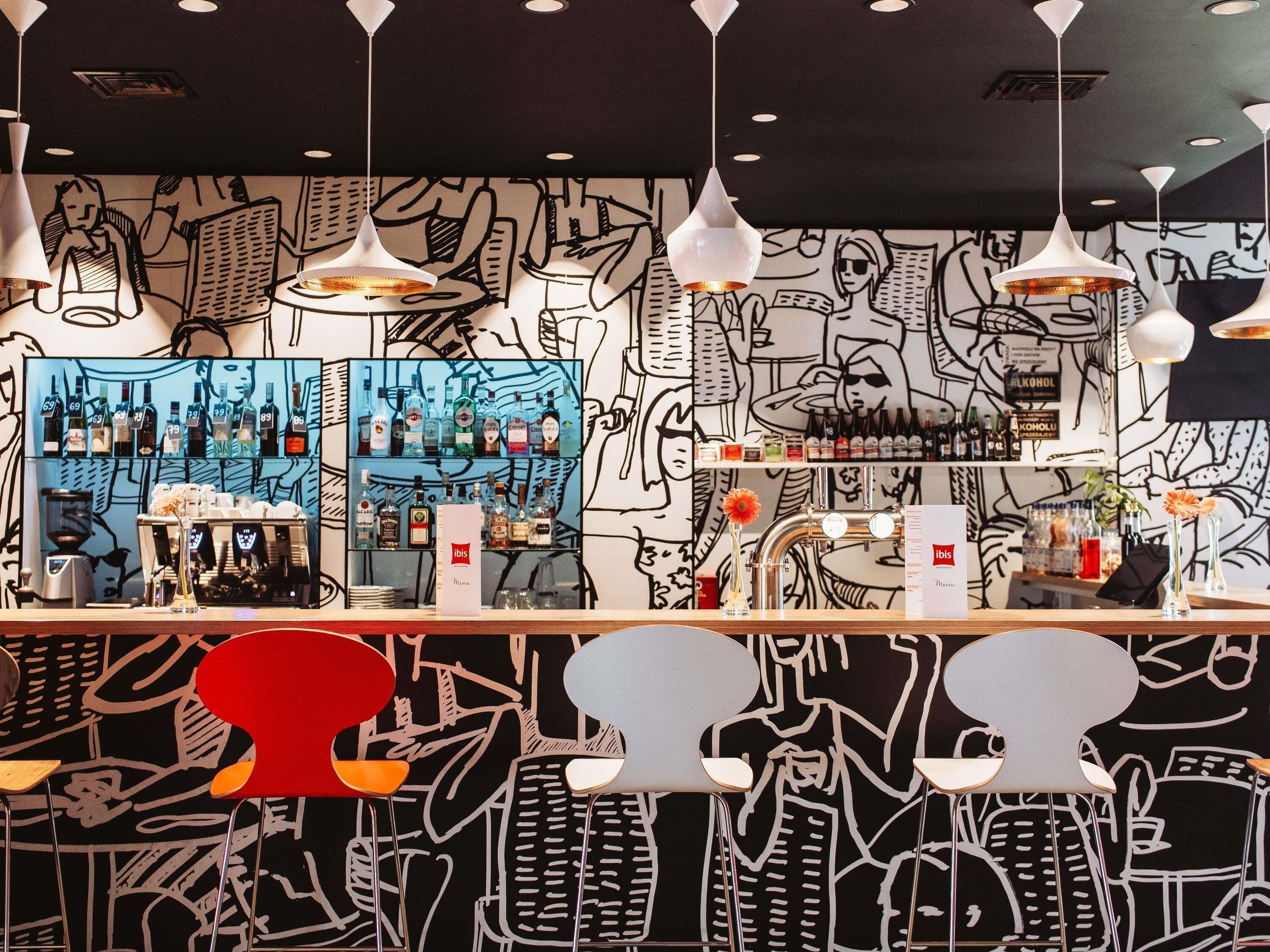 Uma área de bar com design moderno, incluindo um balcão, luminárias pendentes e uma parede com desenhos abstratos em linha.