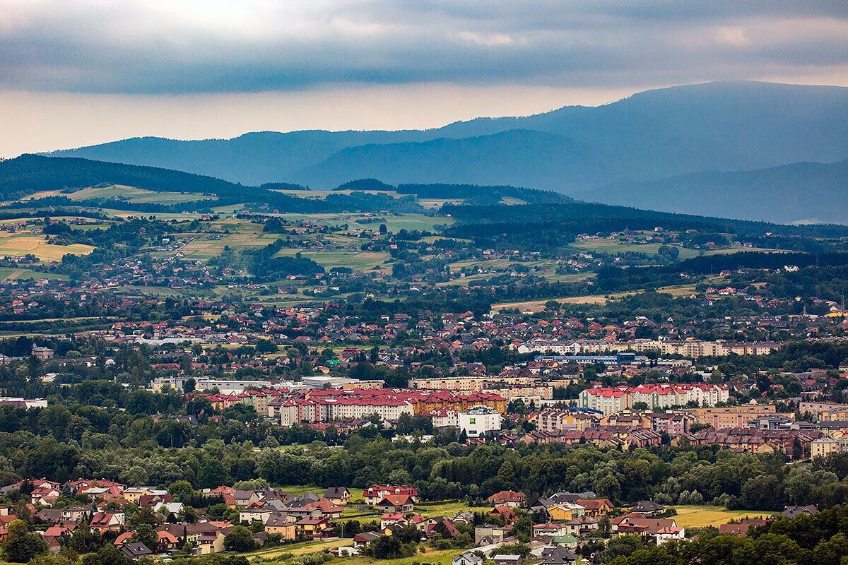 Uma cidade com mistura de edifícios residenciais e comerciais, cercada por colinas e montanhas verdes.