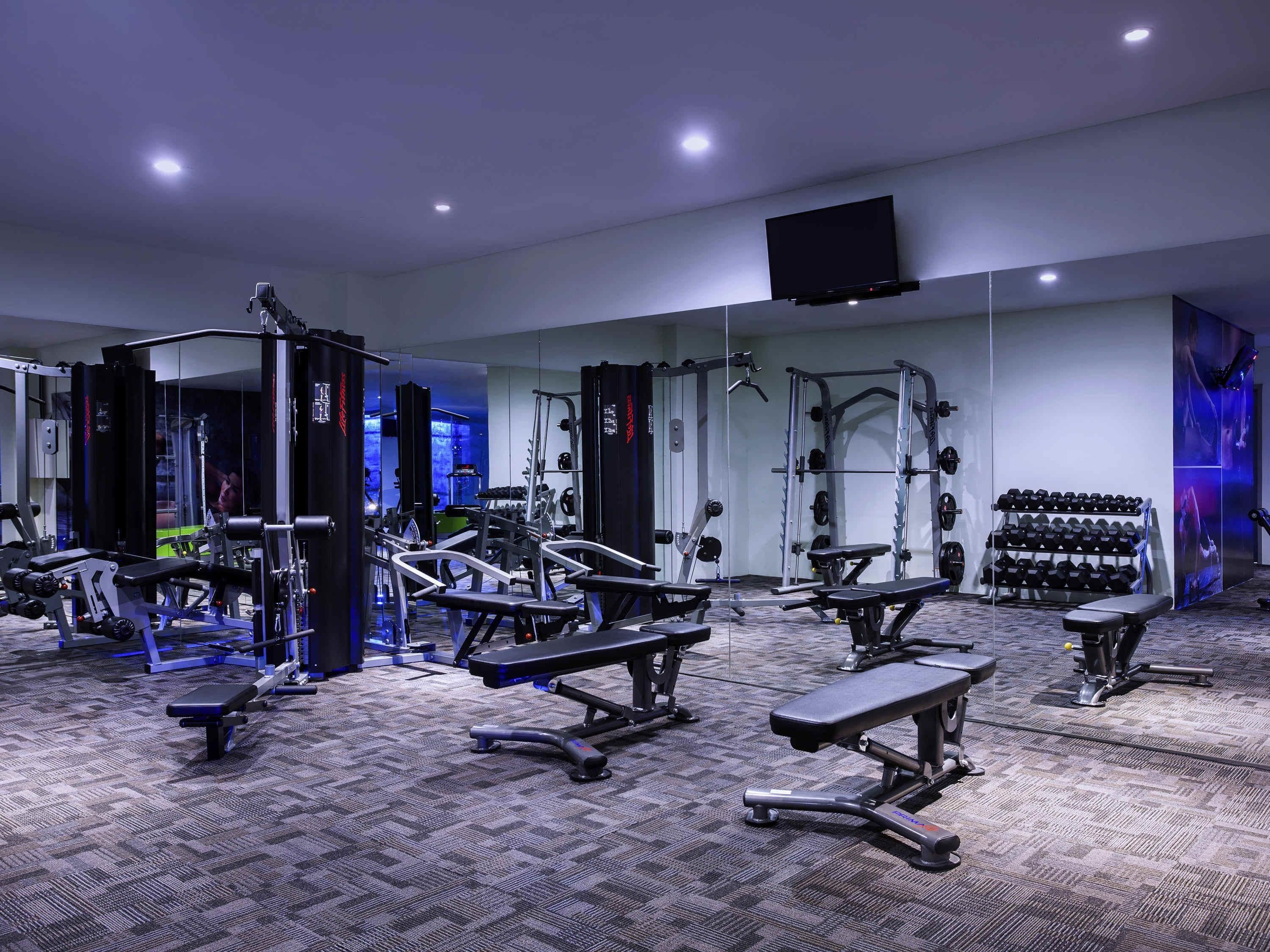 Academia com diversos equipamentos de exercício, incluindo bancos, aparelhos de musculação e halteres.