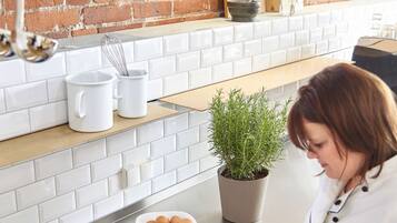 Cozinha com parede de tijolos, azulejos brancos, fogão, frigideira, tigela com ovos e planta em vaso.