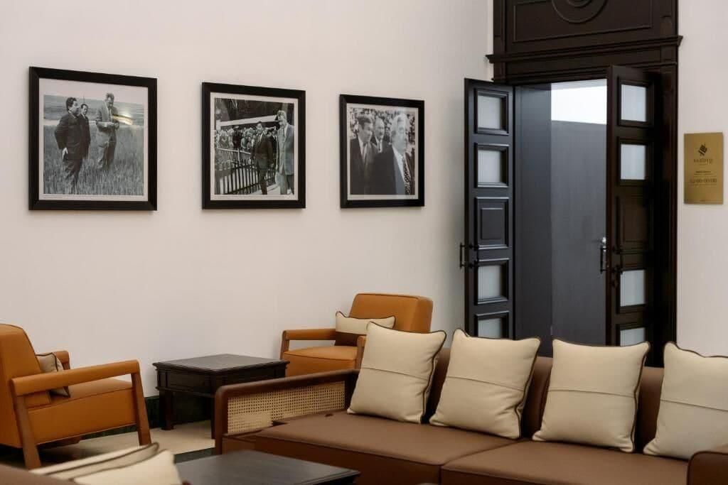 Quarto com sofá, cadeiras e uma mesa. Três fotografias emolduradas na parede.
