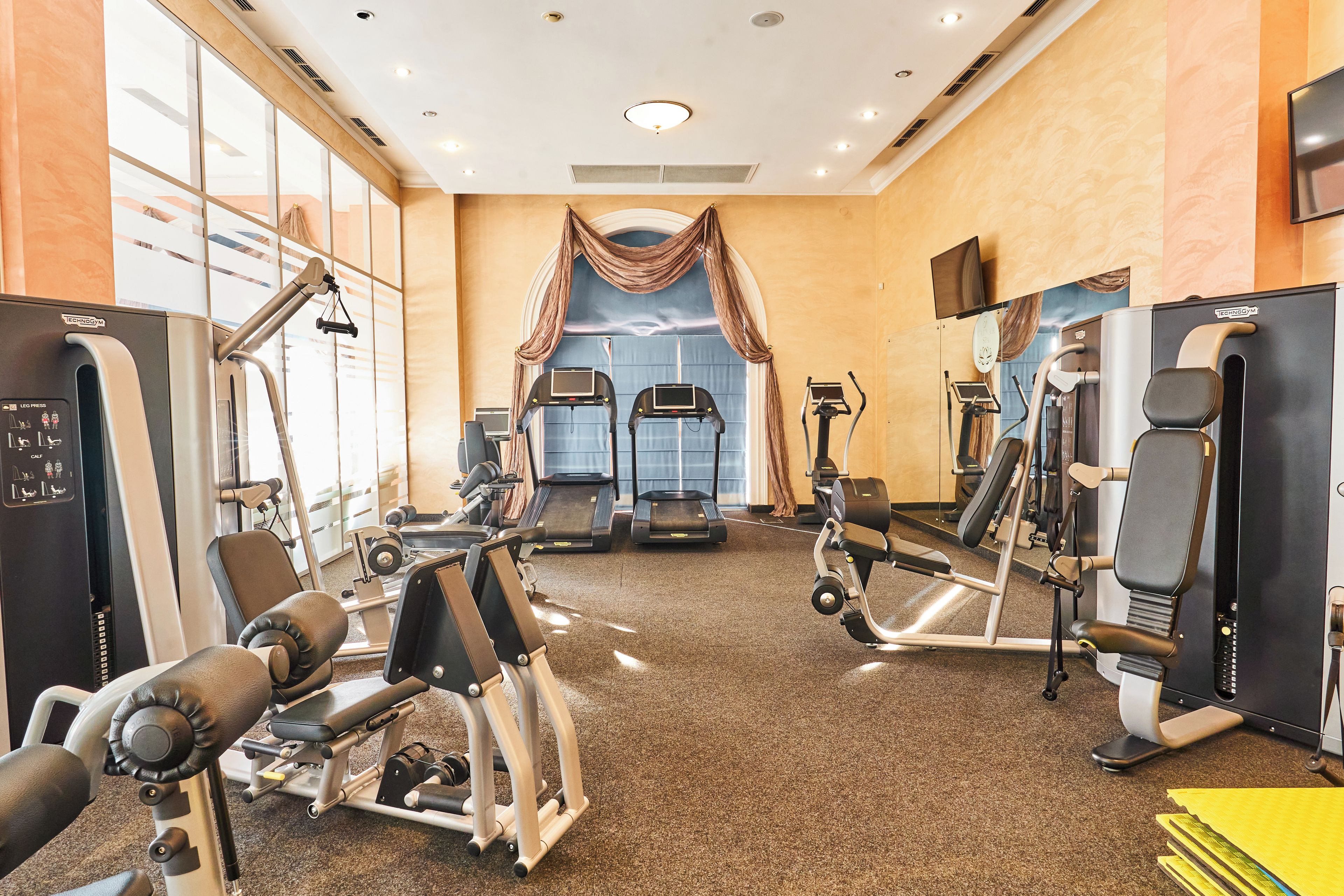 Uma academia com esteiras, máquinas de musculação e um painel de espelhos.