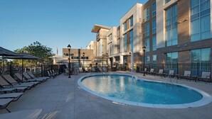Um hotel moderno com piscina, espreguiçadeiras e um pátio coberto.