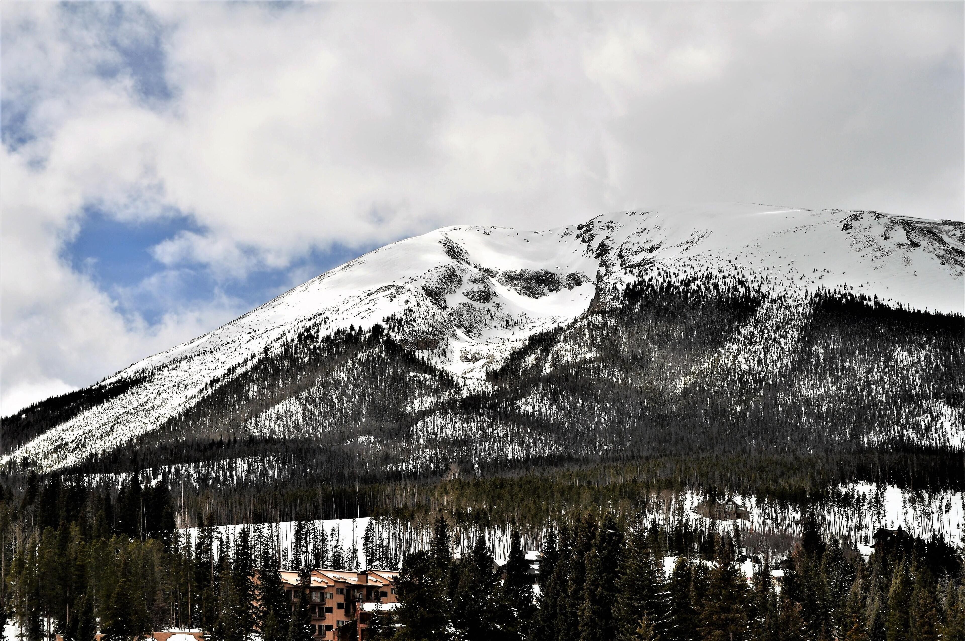 Montanha coberta de neve com um vale arborizado e um edifício na base.